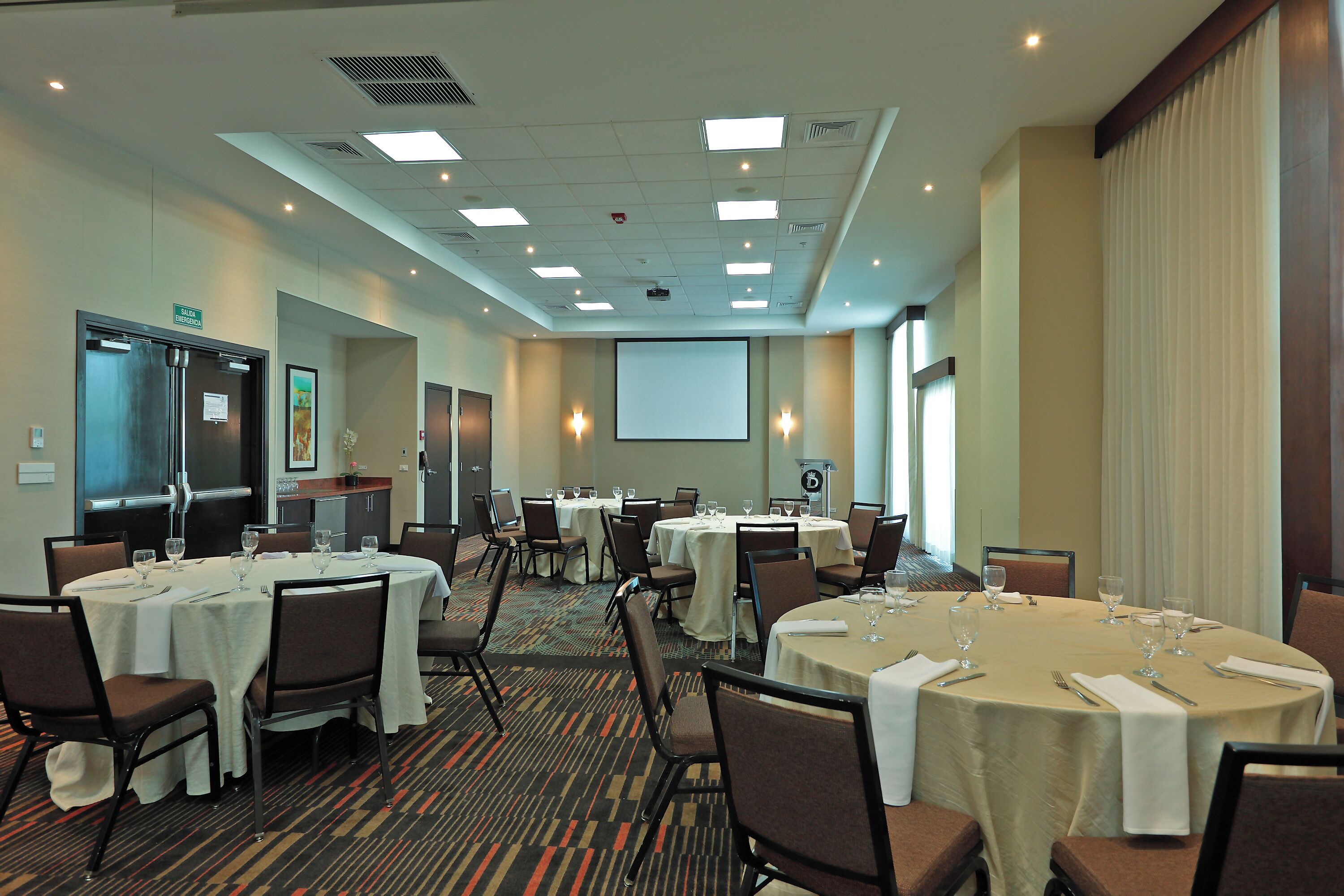 Sala de conferências com várias mesas, cadeiras e um projetor.