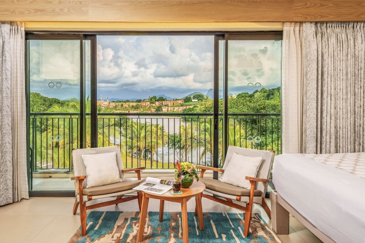 Quarto de hotel com varanda, duas cadeiras, uma mesa pequena e uma cama.