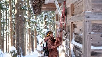 Uma cabana de madeira com fachada coberta de neve e uma pessoa vestindo casaco de inverno e gorro.