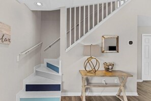 Uma escadaria com corrimão branco, um console de madeira com abajur e um espelho fixado na parede.
