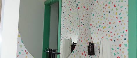 Um banheiro com espelho redondo, pia rosa e porta verde.