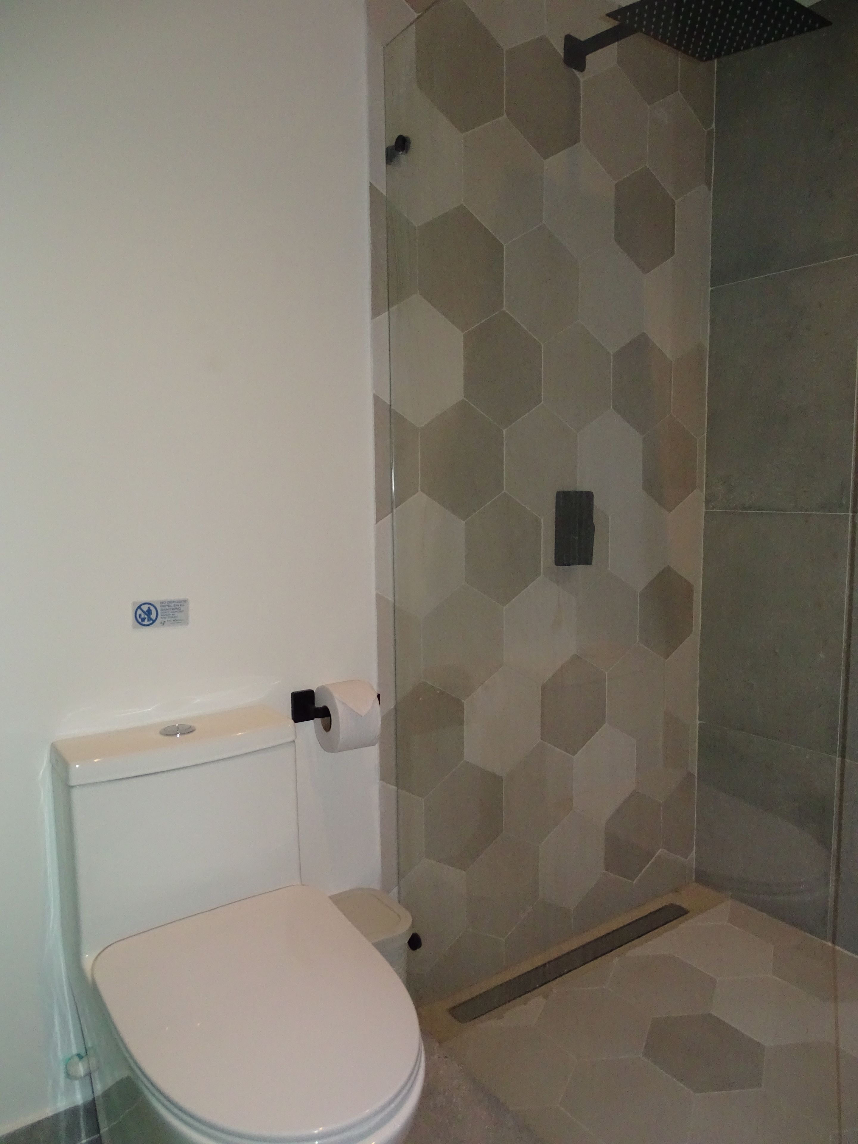 Um banheiro moderno com vaso sanitário, box de chuveiro em vidro e padrão de azulejos hexagonais nas paredes.