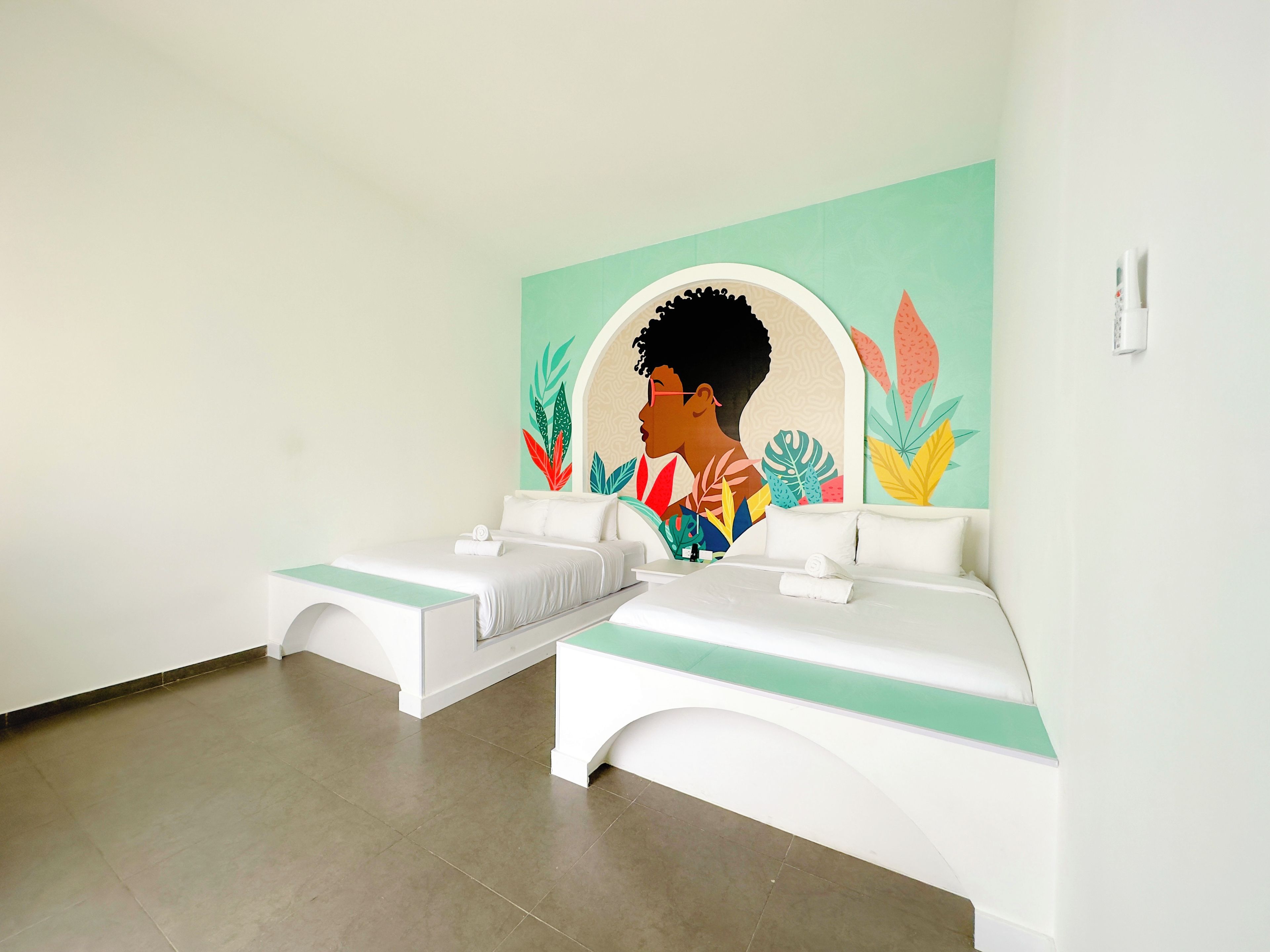 Quarto com duas camas, um mural na parede e banheiro com porta-toalhas.