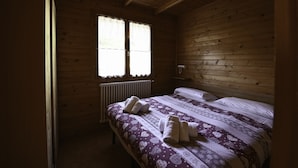 Quarto de cabana de madeira com cama, duas toalhas, radiador e janela com cortinas.
