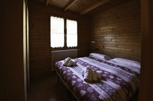 Quarto de cabana de madeira com cama, duas toalhas, radiador e janela com cortinas.