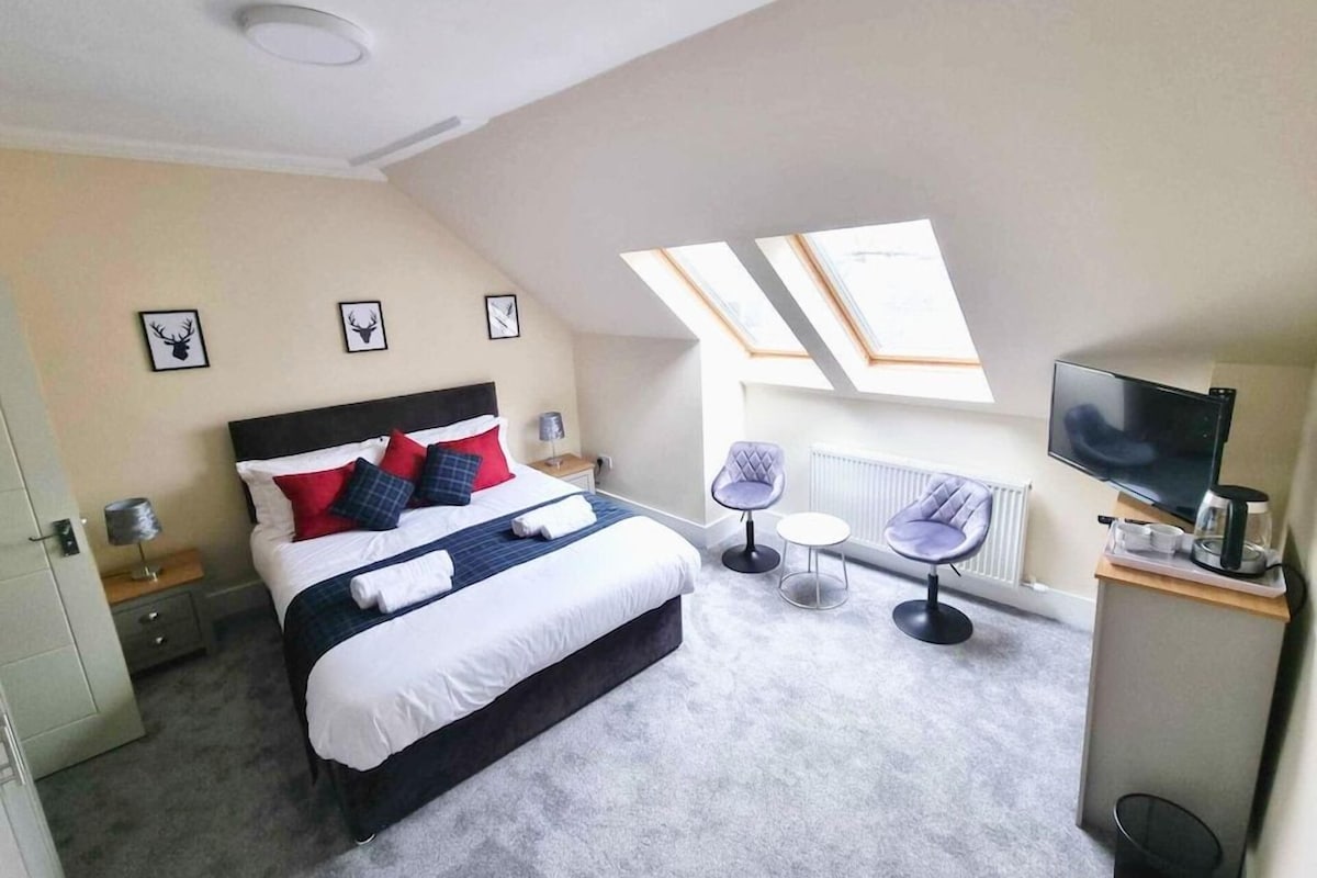 Quarto com cama, televisão, mesinha e cadeira.