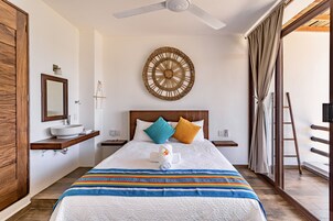 Quarto de hotel com cama, decoração circular na parede, cabeceira de madeira, mesa de cabeceira, cortinas numa janela e piso de madeira.