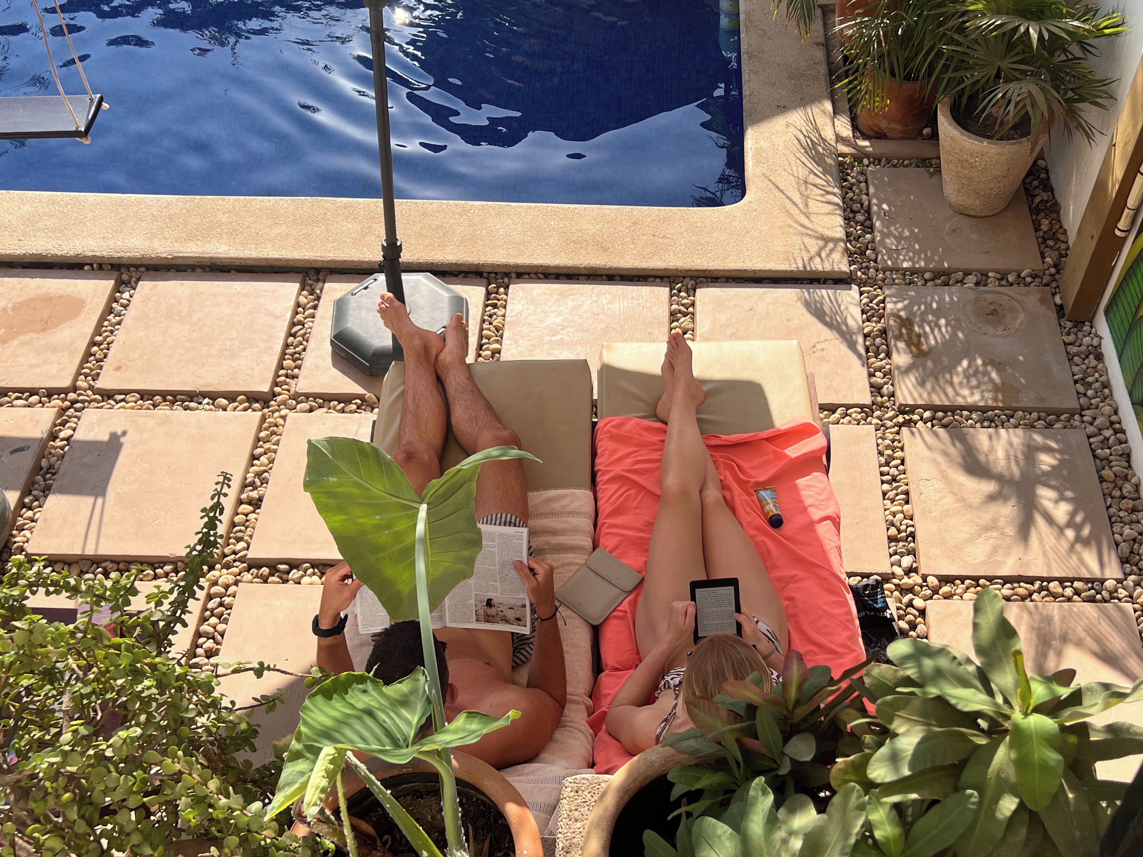 Área de piscina com espreguiçadeiras, piscina e plantas em vasos.