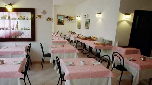 Uma área de refeições com mesas cobertas por toalhas cor-de-rosa, cadeiras e luminárias fixadas na parede.