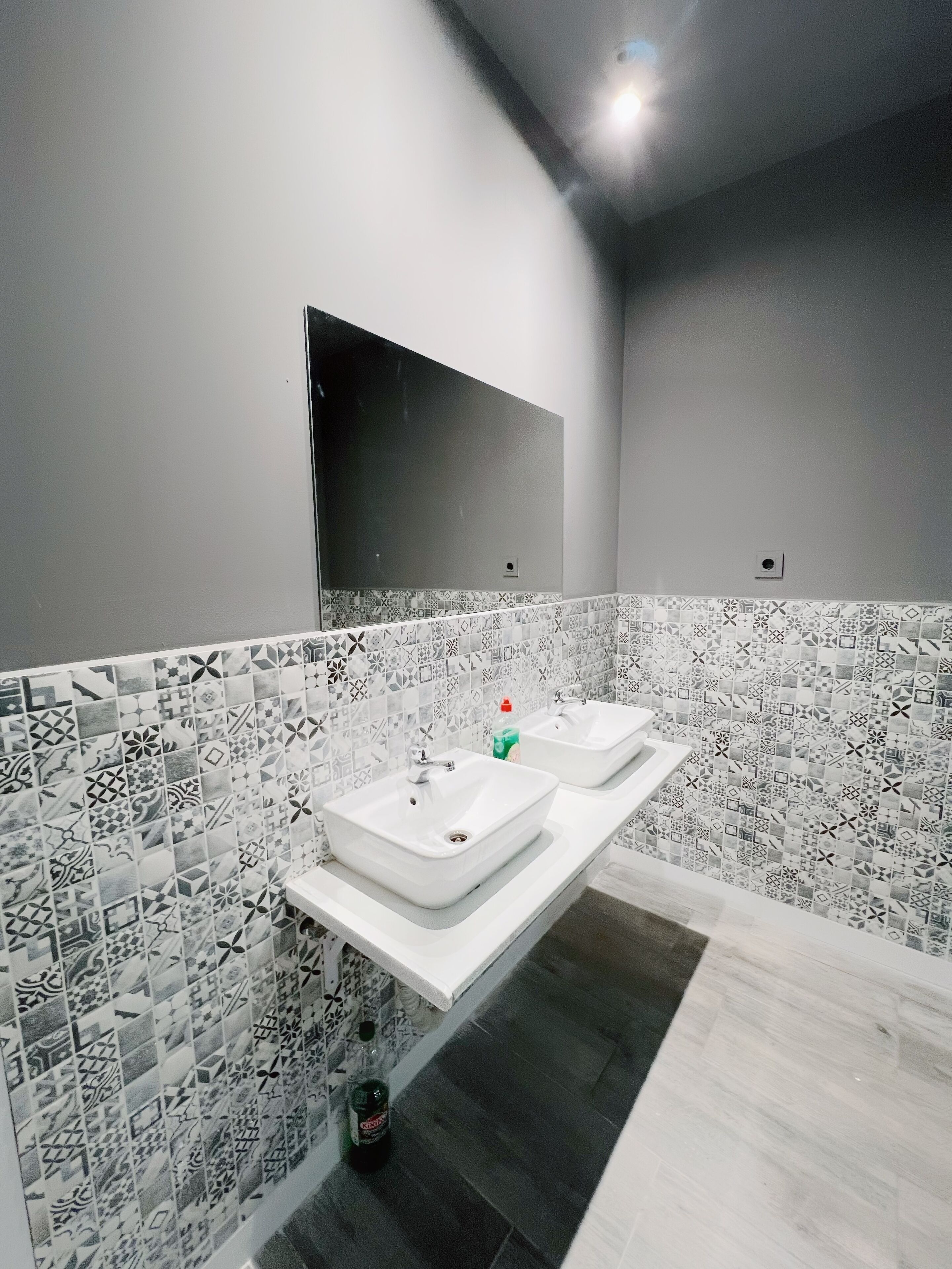 Um banheiro com duas pias, um espelho e azulejos estampados.