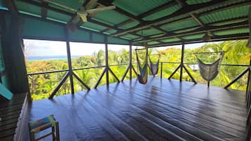 Quarto com vista para uma paisagem exuberante, uma rede e um banco de madeira.