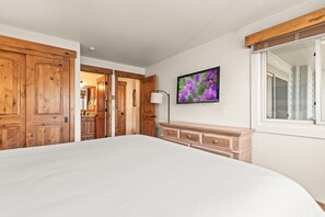 Quarto com portas de madeira, uma cama, cômoda, televisão e janela.
