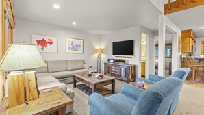 Uma sala de estar com sofá, duas poltronas, uma mesa de centro e TV na parede.