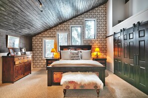 Quarto com teto inclinado, cama de madeira, cômoda e guarda-roupa.