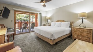 Quarto com cama, escrivaninha, cadeira, mesa de cabeceira e luminária. Há um ventilador de teto e uma janela com vista para o exterior.