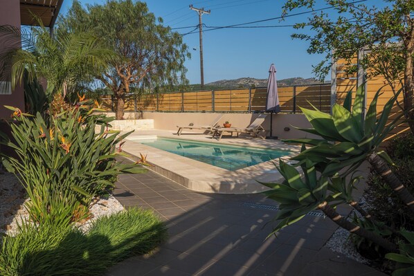 Piscina com espreguiçadeiras, rodeada por plantas tropicais e uma cerca de madeira.