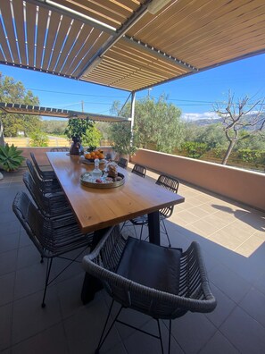 Um pátio externo com mesa de madeira, cadeiras de vime e um vaso com planta.