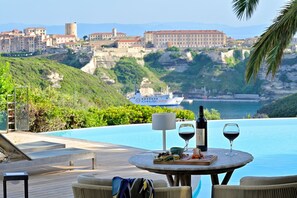 Área da piscina com mesa posta para dois, uma garrafa de vinho e um copo de vinho tinto.