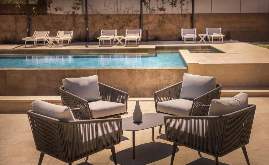Uma área à beira da piscina com cadeiras de vime e uma pequena mesa, rodeada por espreguiçadeiras e uma piscina.