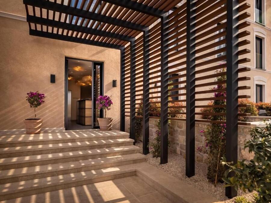 Uma entrada de edifício moderna com um alpendre coberto, degraus que levam à porta e plantas em vasos.
