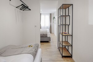 Um corredor estreito, com uma cama à esquerda e uma estante de livros à direita.