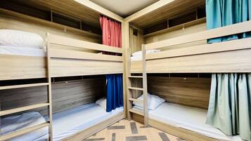Quarto com beliches de madeira, piso em padrão herringbone e cortinas em vermelho, azul e verde-água.