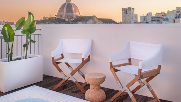 Terraço no telhado com banheira de hidromassagem, duas poltronas brancas acolchoadas, uma mesinha redonda e um vaso de plantas.