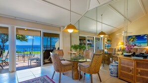 Uma ampla sala de jantar com mesa de vidro e cadeiras de vime, com vista para a piscina e para o oceano.