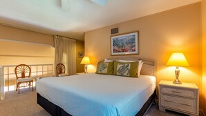 Quarto de hotel com uma cama grande, duas mesas de cabeceira com luminárias, uma cadeira, um quadro na parede e uma janela com cortinas.