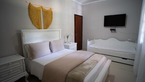 Quarto com cama, mesa de cabeceira, penteadeira, televisão e porta.