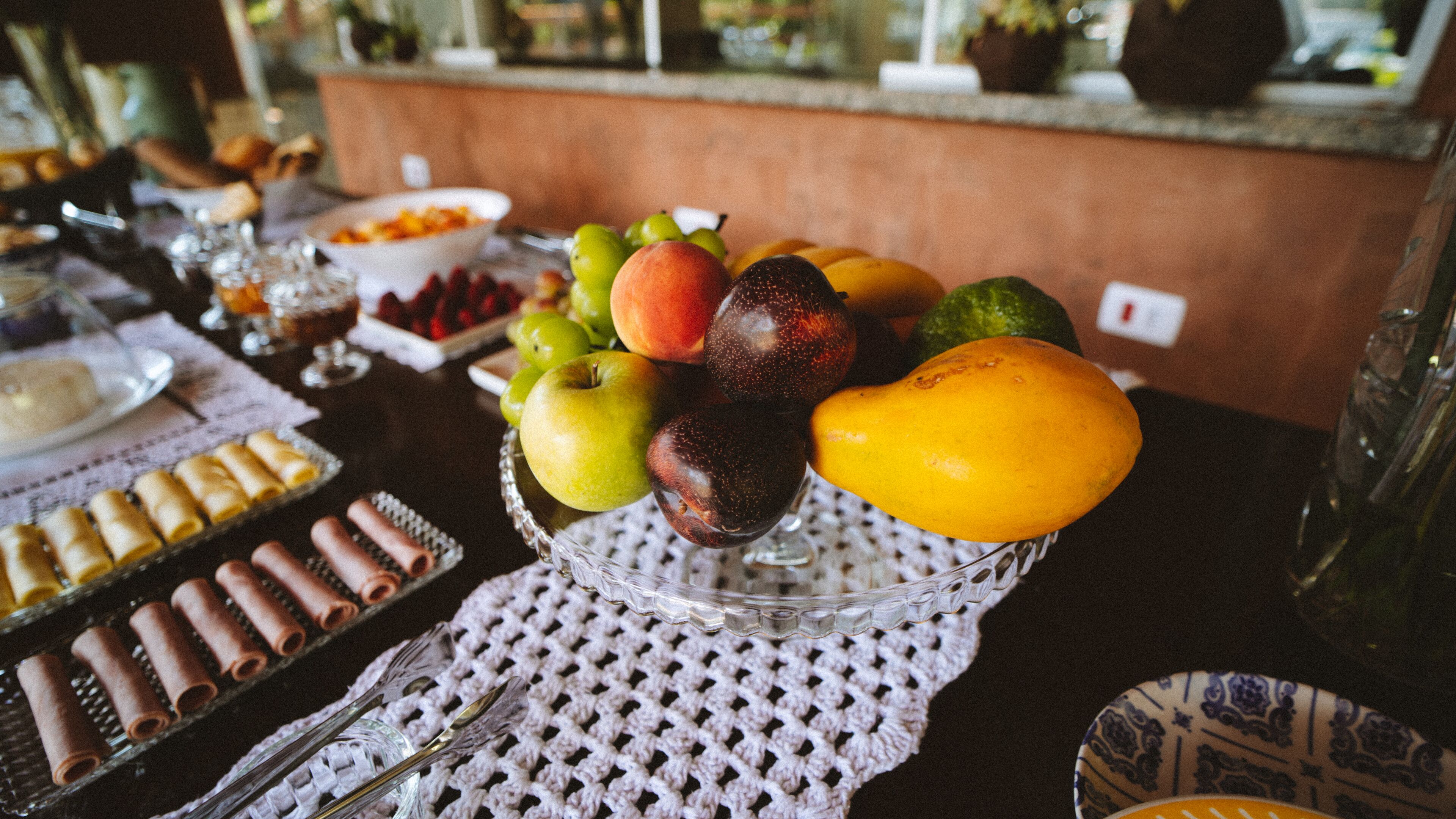 Uma mesa com uma tigela de frutas, doces e um jogo americano de crochê.