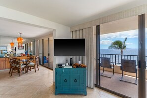 Quarto de hotel com varanda, área de refeições e televisão na parede.