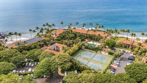 Vista aérea de um resort com praia, painéis solares, quadras de tênis e área de estacionamento.