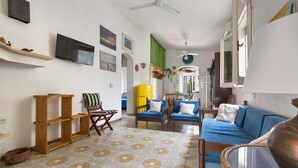 Uma sala de estar com piso estampado, um sofá azul, móveis de madeira e uma TV fixada na parede.