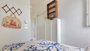 Quarto com cama, guarda-roupa, bolsa pendurada e prateleira com uma planta.