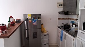 Uma cozinha compacta com geladeira de aço inoxidável, armários brancos e piso ladrilhado.