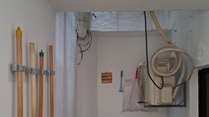 Casa de banho com lavatório, um balde verde para limpeza e várias ferramentas de limpeza como esfregões e uma mangueira.