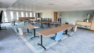 Uma sala de conferências com várias mesas e cadeiras, uma copa e uma janela grande.