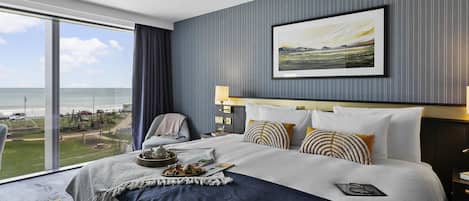 Quarto de hotel com uma cama grande, vista para a praia e um quadro na parede.