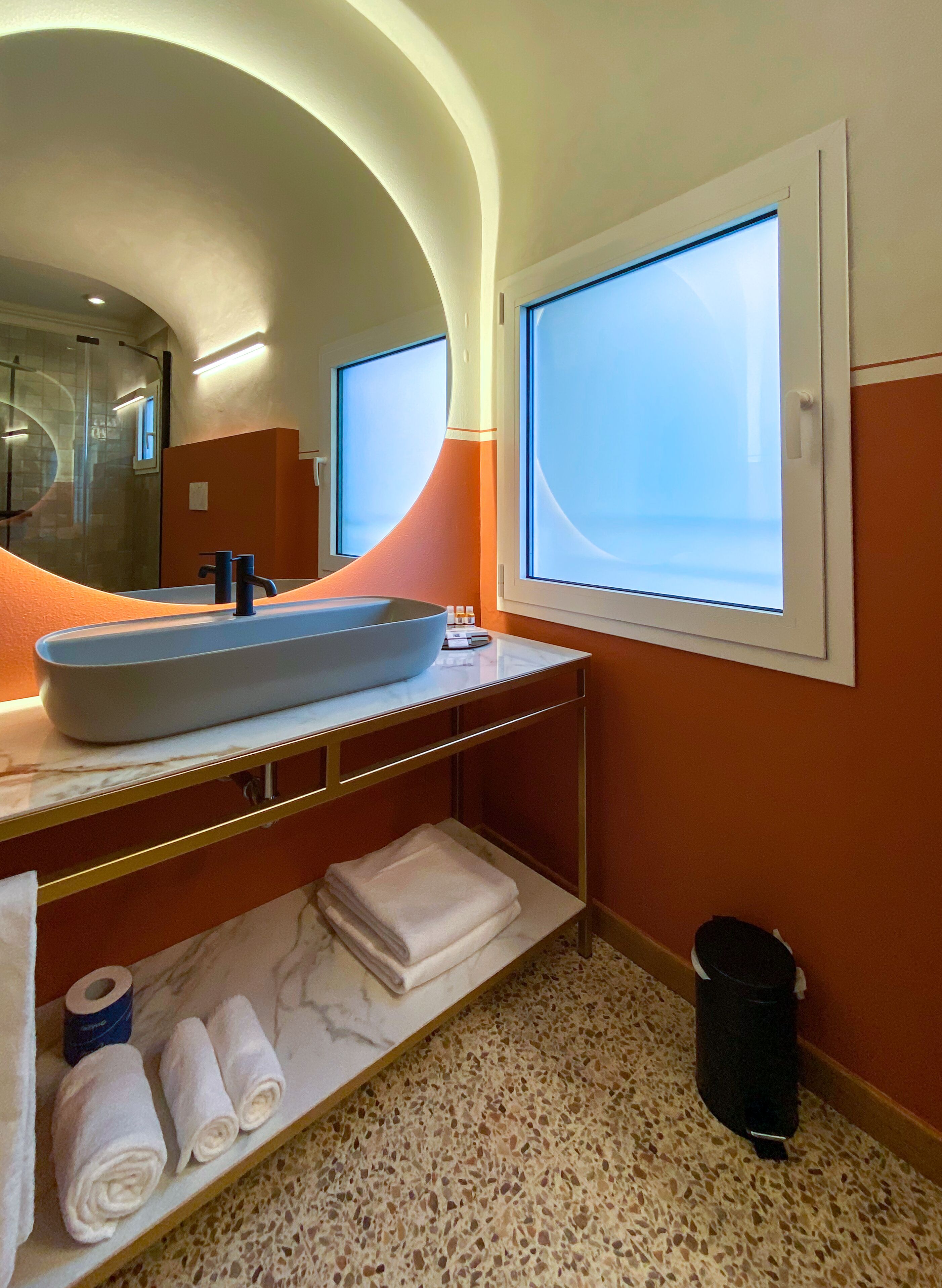 Uma casa de banho moderna com uma grande lavatório oval, um espelho e uma janela.