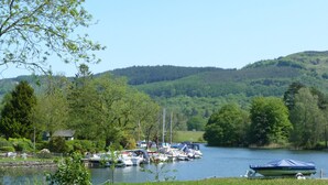 Vista para o lago com barcos atracados, rodeada por vegetação exuberante e colinas ao fundo.