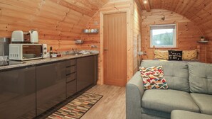 Interior acolhedor de uma cabana com cozinha compacta, um sofá e uma janela.