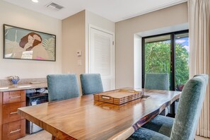 Uma sala de jantar com uma mesa de madeira, duas cadeiras, um quadro na parede e uma janela com vista para o verde.