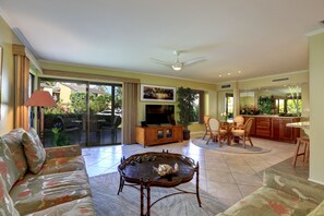 Uma sala de estar com sofá, mesa de centro, televisão e um espaço de jantar com cadeiras e mesa.