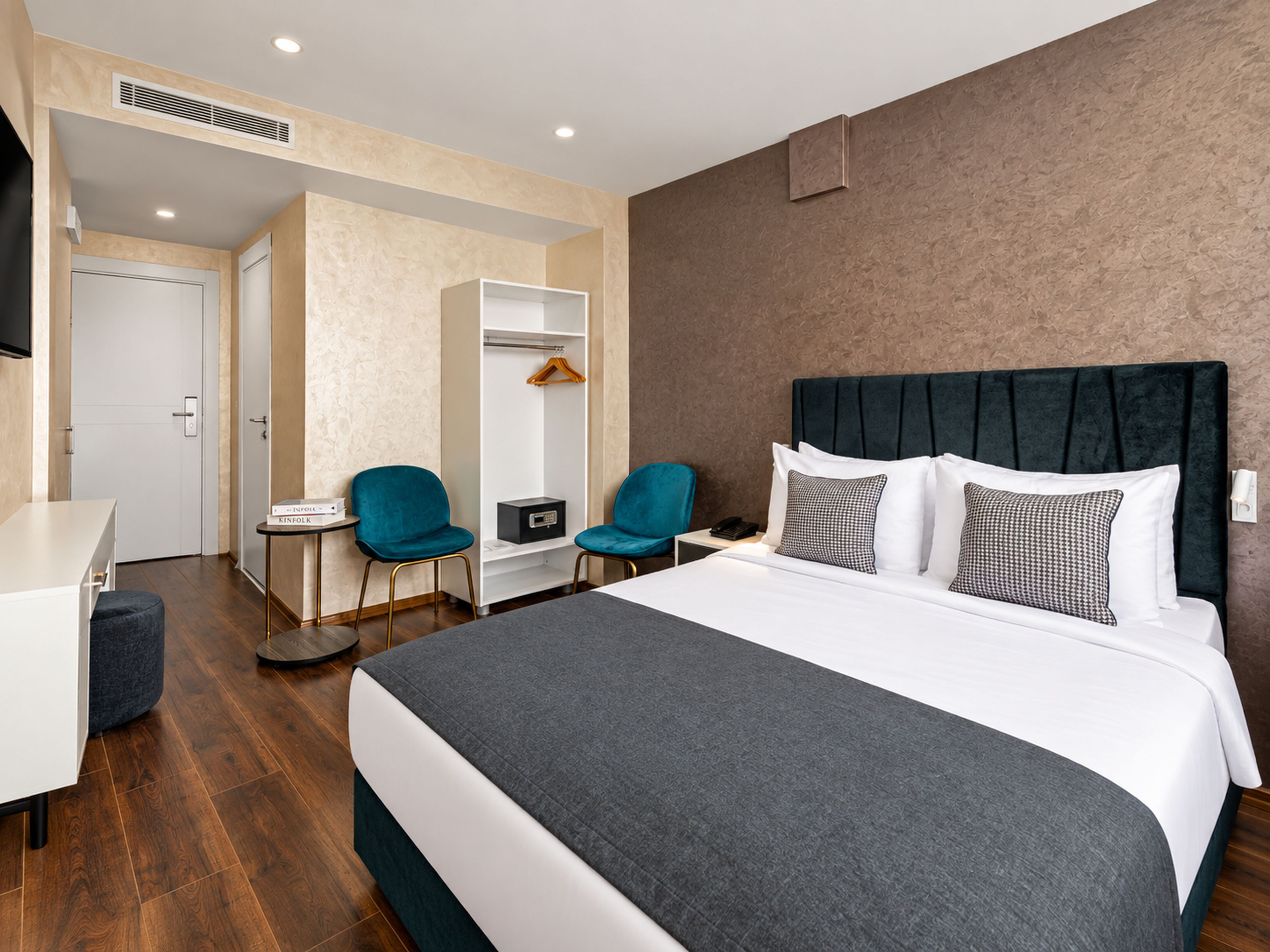 Quarto de hotel com cama, duas cadeiras, escrivaninha, guarda-roupa e televisão.