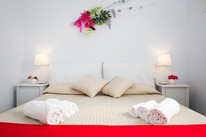 Cama bem arrumada com duas almofadas, duas mesas de cabeceira com luminárias e um arranjo de flores na parede.