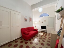 Uma sala de estar com um sofá vermelho, uma televisão, um abajur e uma mesa redonda.