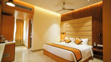Quarto de hotel com uma cama grande, uma escrivaninha, um ventilador de teto e uma cabeceira de madeira.