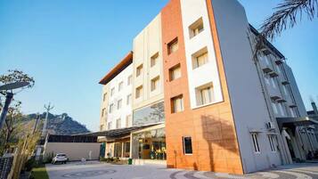 Um hotel de vários andares com design moderno, apresentando uma combinação de fachadas brancas e marrons, grandes janelas e uma área de entrada coberta.