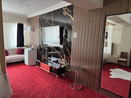 Quarto de hotel moderno com carpete vermelho, sofá, TV, minibar e espelho.